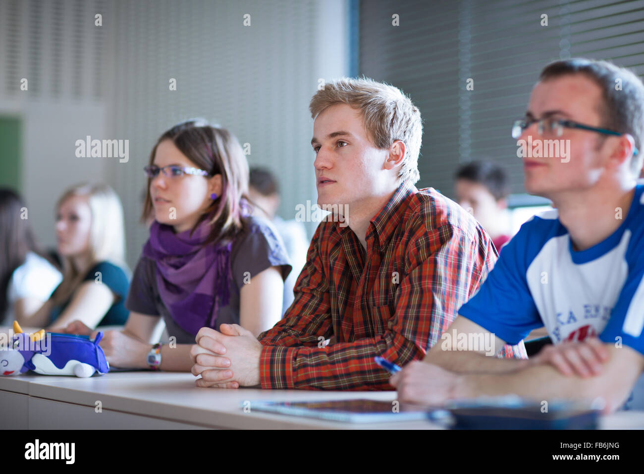 Handsome college student sitting in a classroom full of students during ...