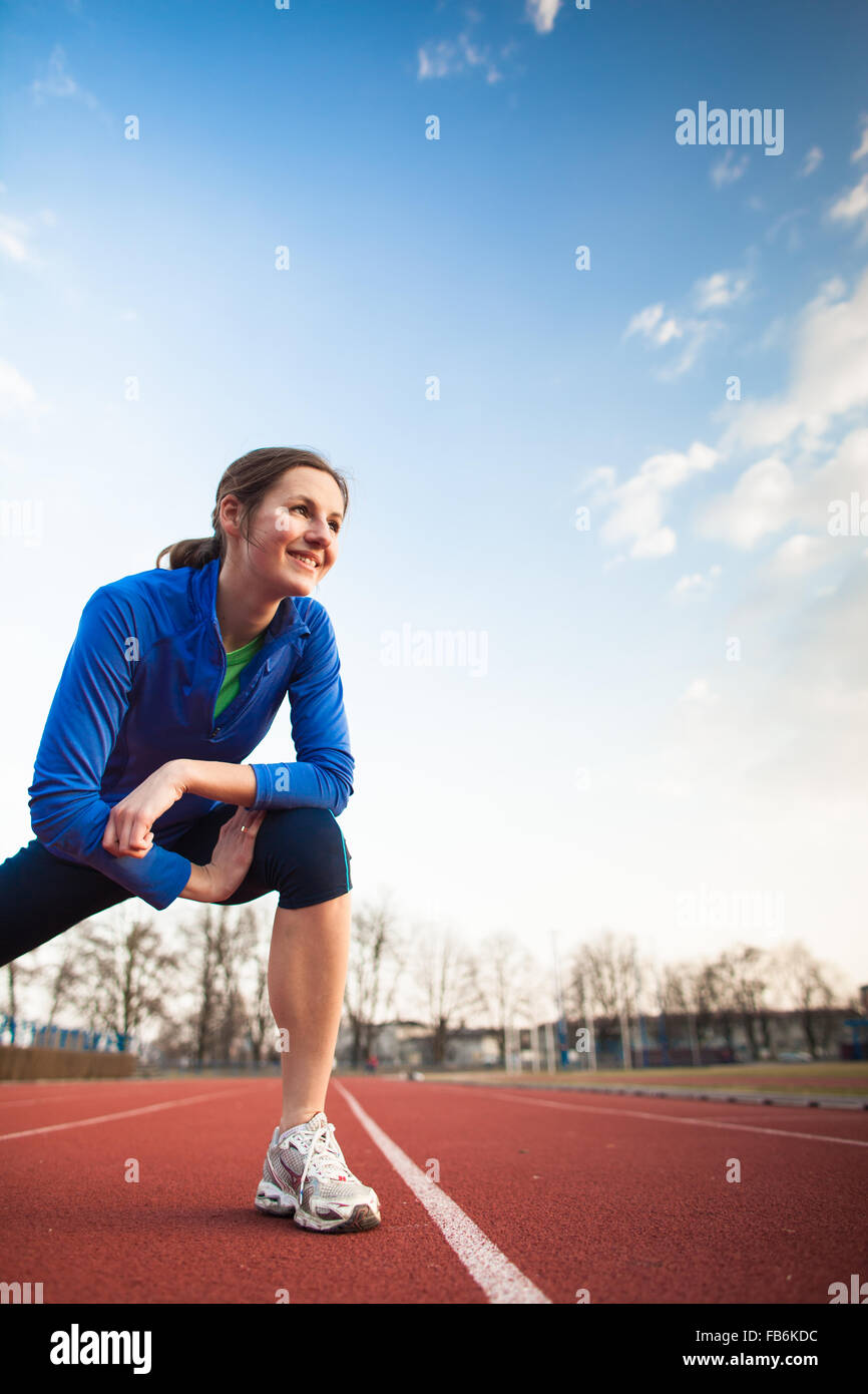 Pretty female runner stretching before her run at a track and field ...