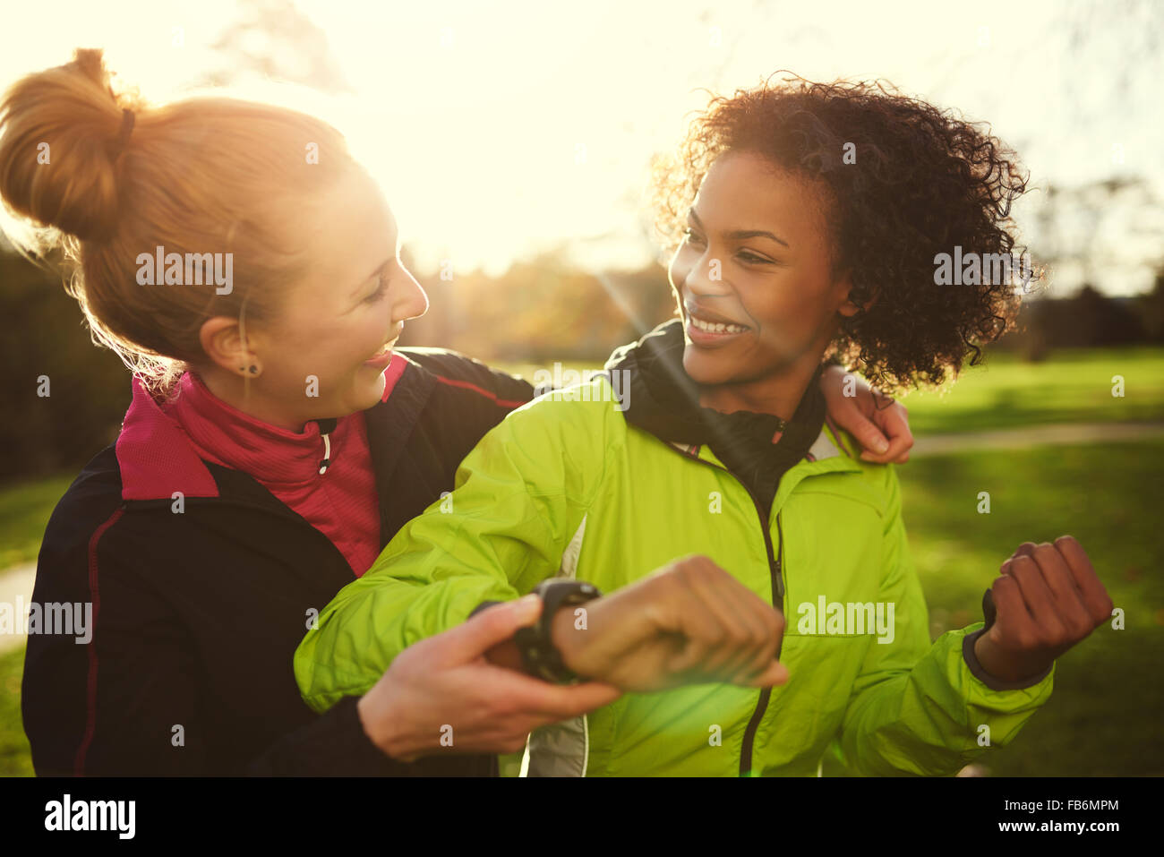 Two female athletes smiling and hugging after workout in sunny park ...