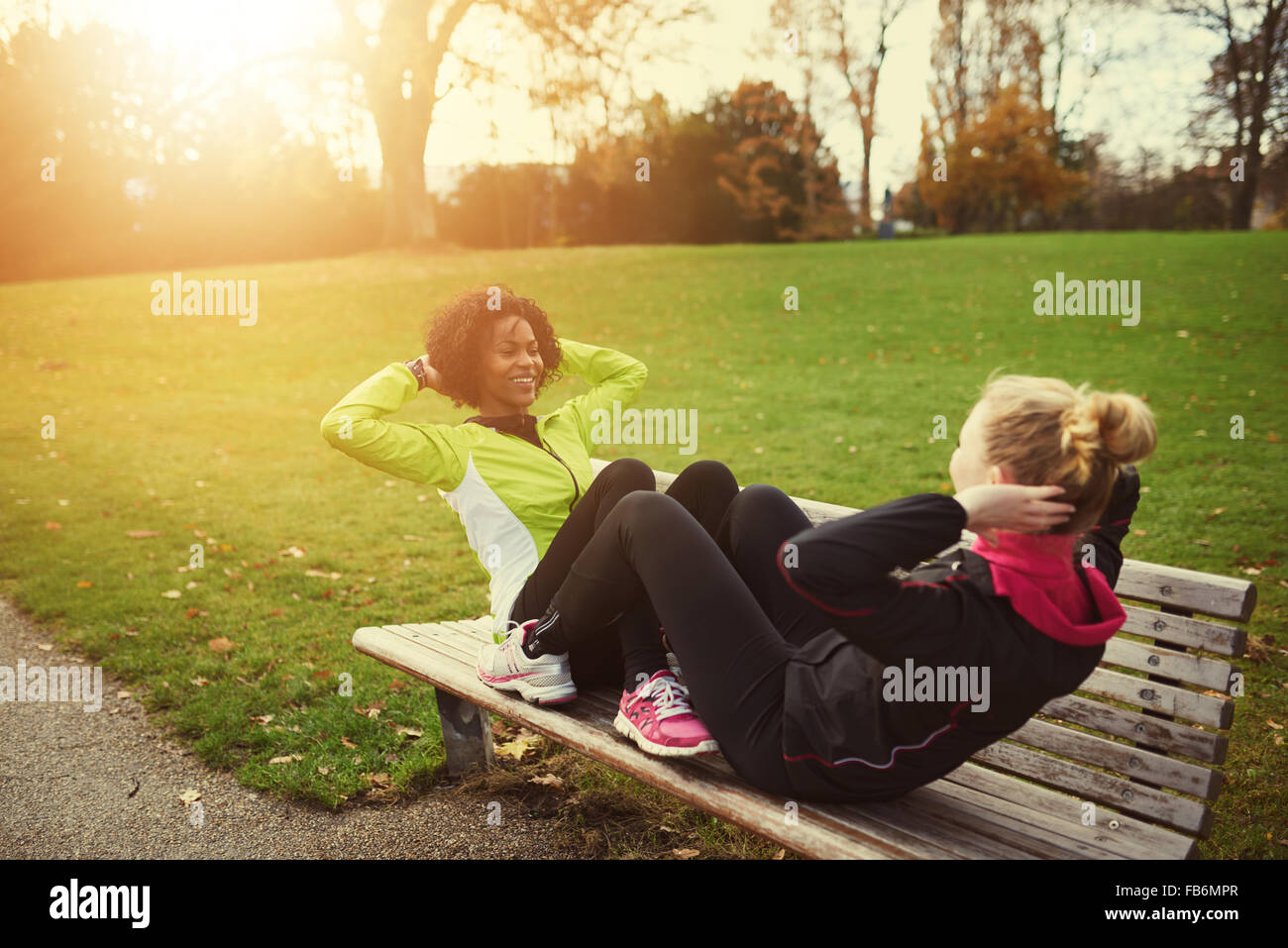 Two female athletes doing sit-ups on bench in park Stock Photo - Alamy