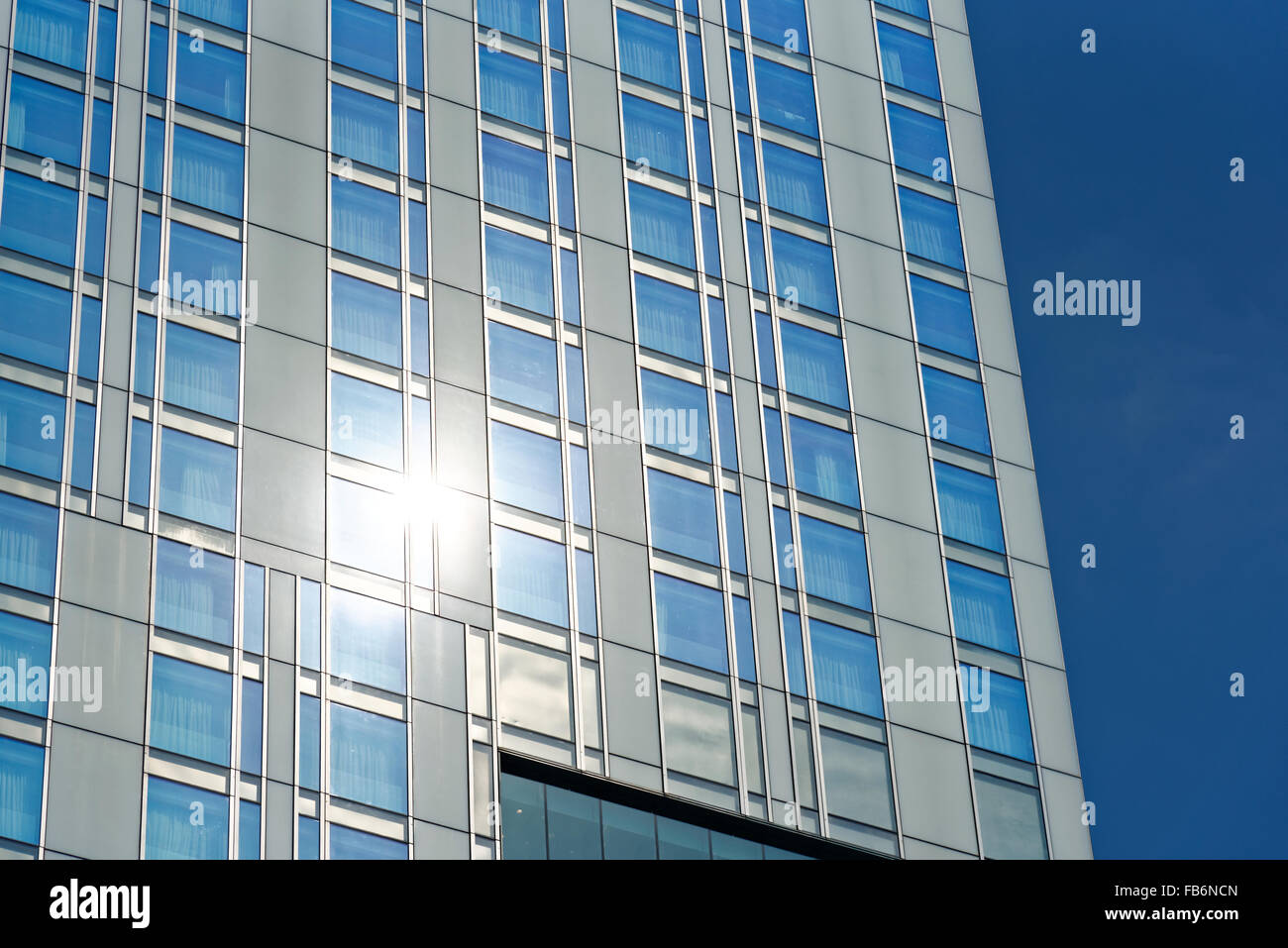 grey Skyscraper with blue windows and a sun flare and blues sky Stock ...