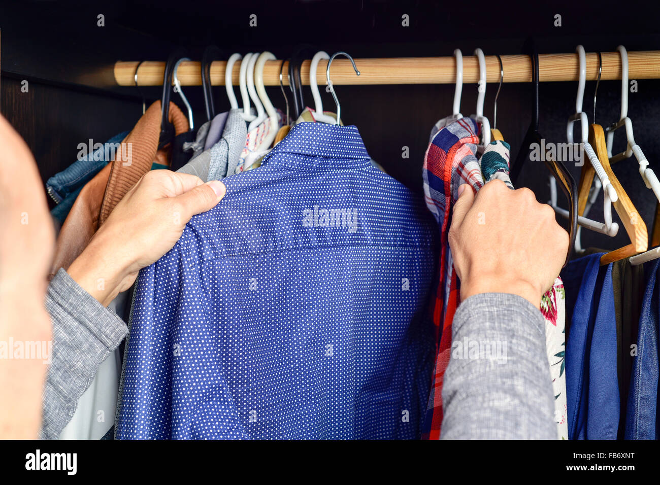 closeup of a young caucasian man choosing a shirt from a clothes rack ...