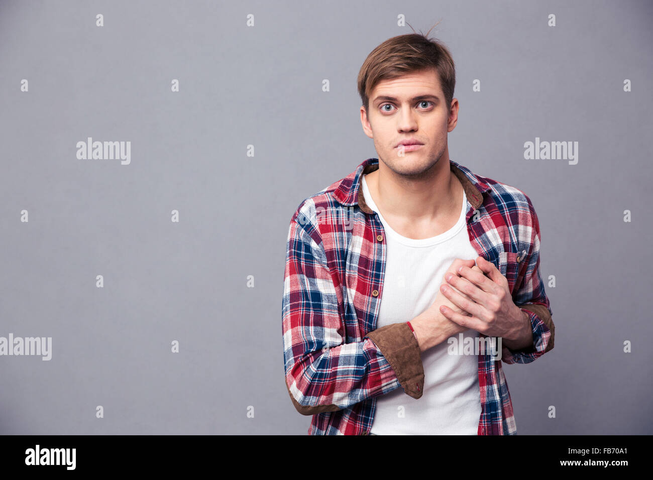 Stunned dazed young man in checkered shirt with hand on chest over grey ...