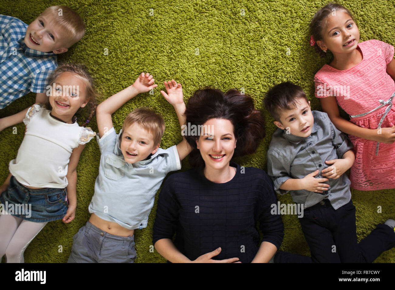 Directly above shot of happy female teacher and students lying on rug ...
