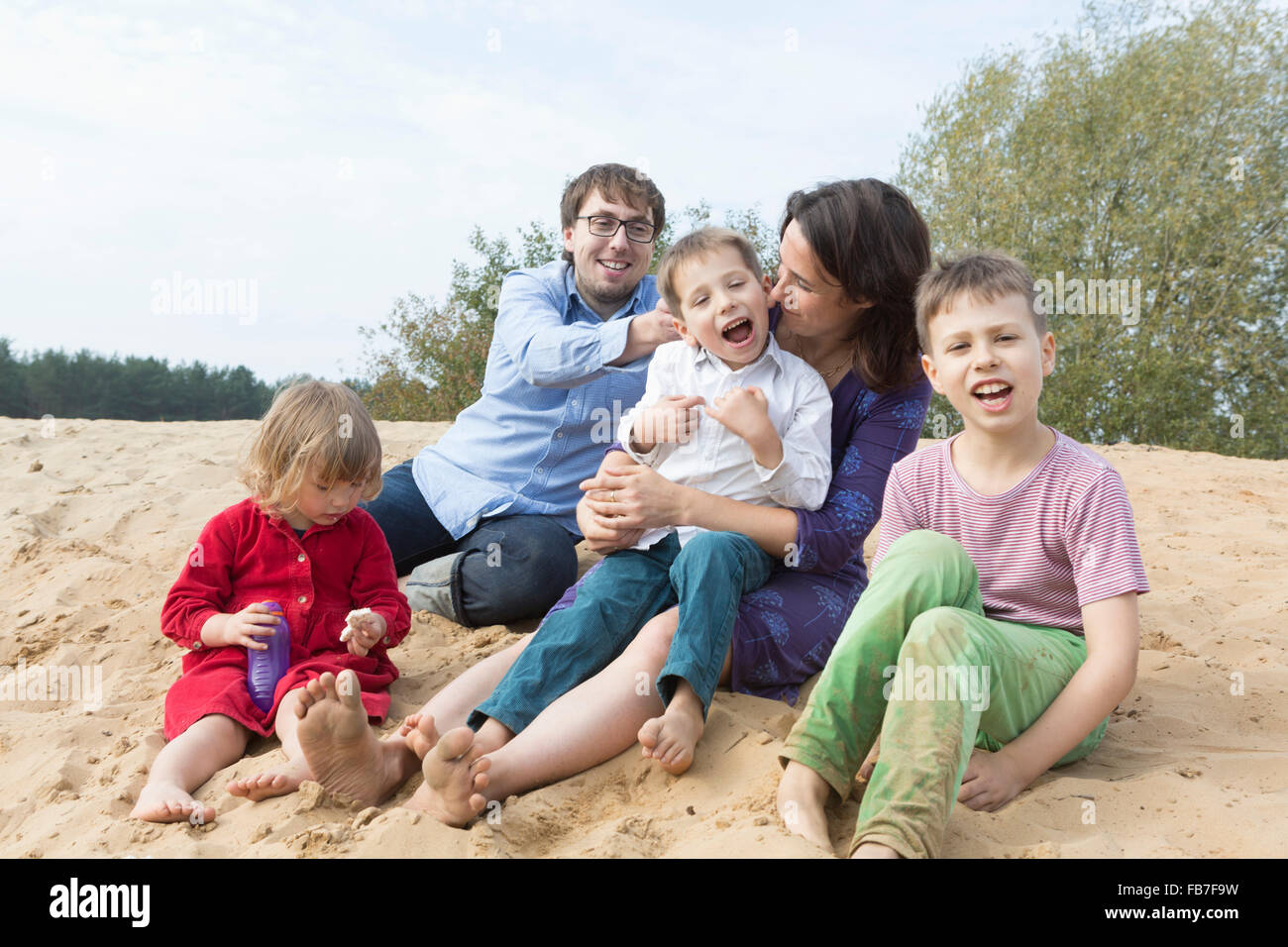 Cheerful family sitting together on sand dune Stock Photo - Alamy