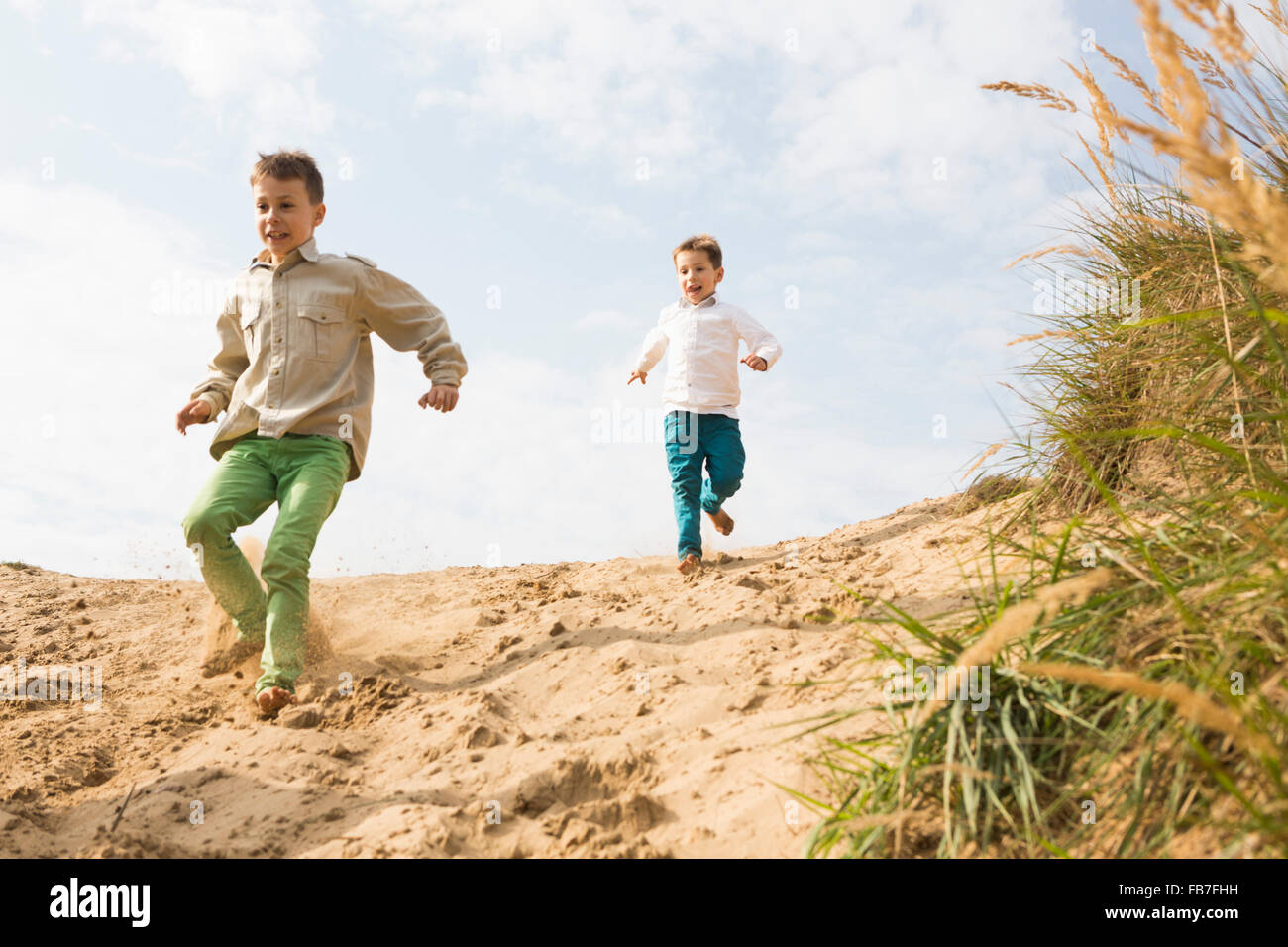 Low angle view of brothers running on sand dune Stock Photo - Alamy