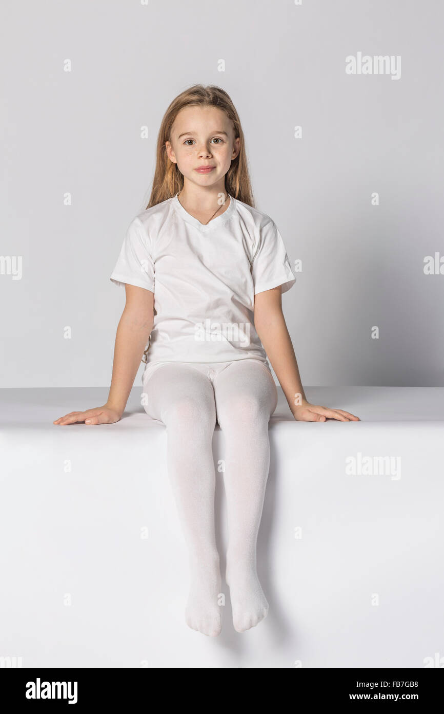 Full length portrait of cute girl sitting against white background ...