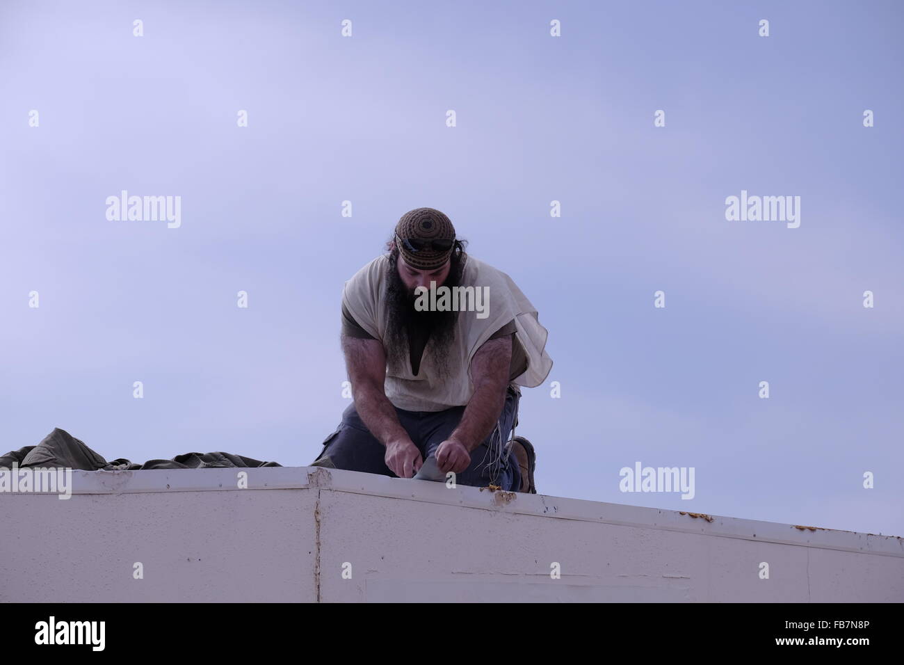 A religious Jewish settler repairs the roof of his temporary home in ...
