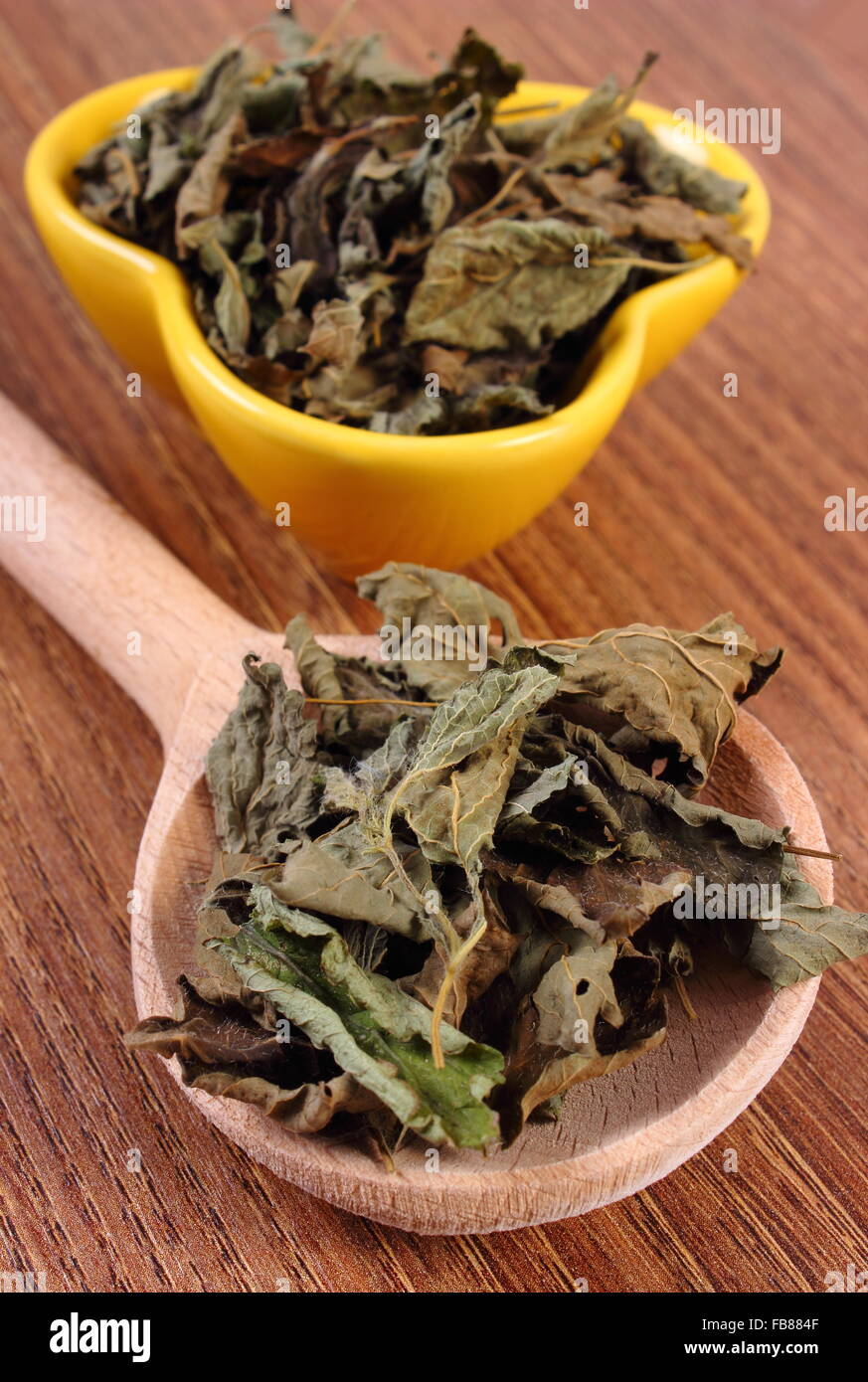 Heap of healthy dried lemon balm with spoon and yellow bowl on wooden ...