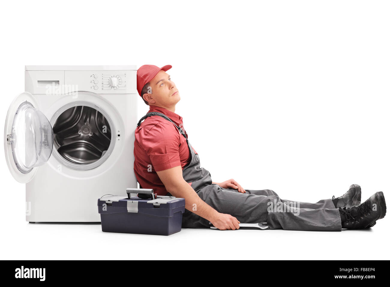 Exhausted young plumber sitting by a washing machine and looking up ...