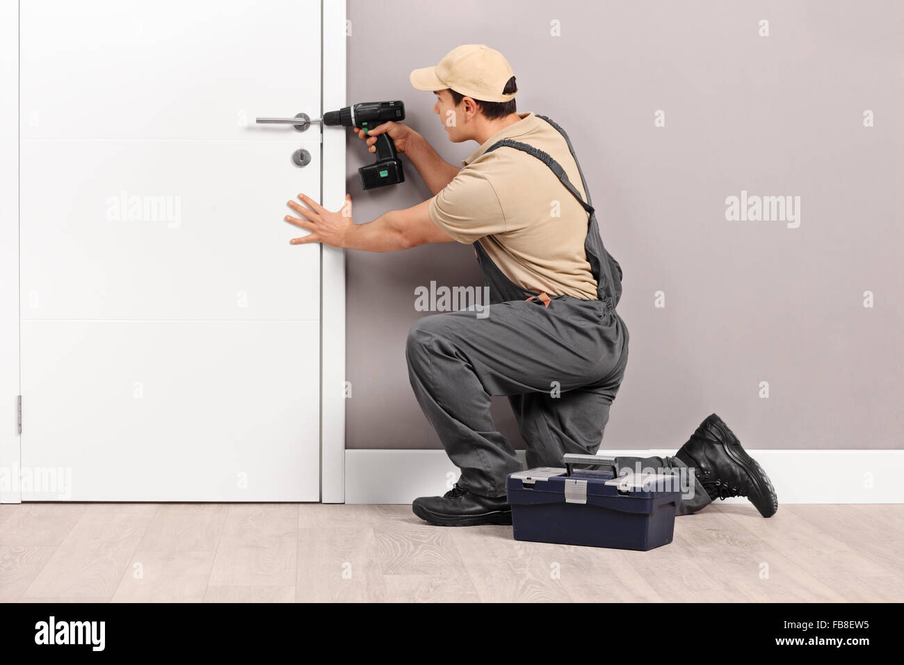 Young male locksmith installing a lock on a new white door with a hand ...