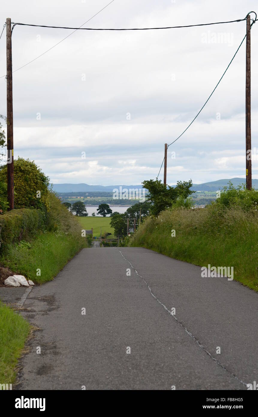 Road crossing under a power cable and going downhill towards the Forth ...