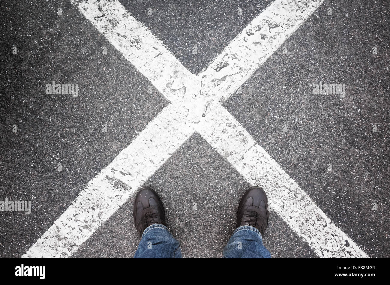 Male feet standing on dark urban asphalt with crossing lines of road ...