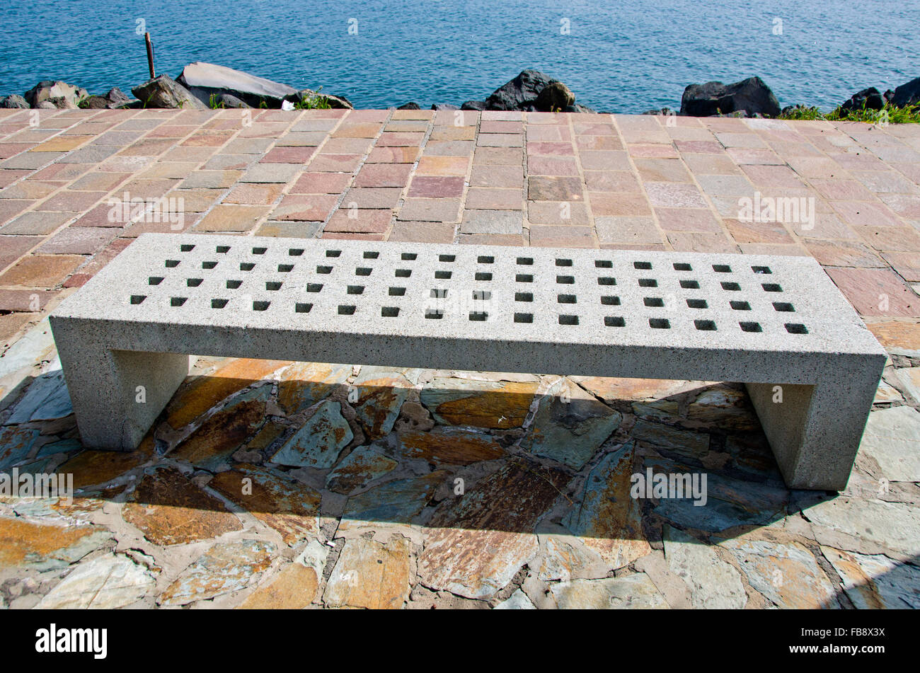 Rectangular cement bench with square holes on the stone pavement by the ...