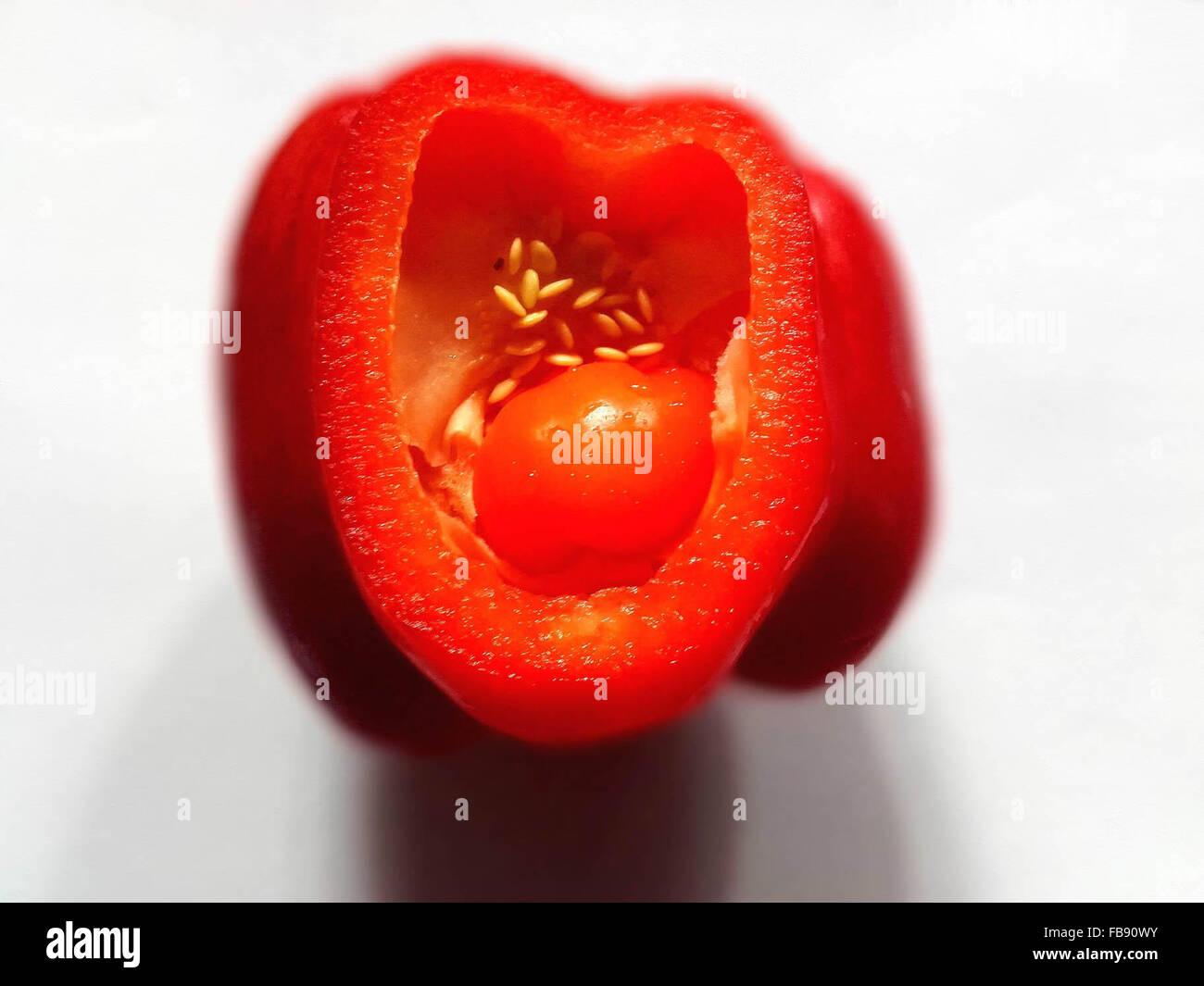 Cut open red bell pepper with another pepper growing inside on a white ...
