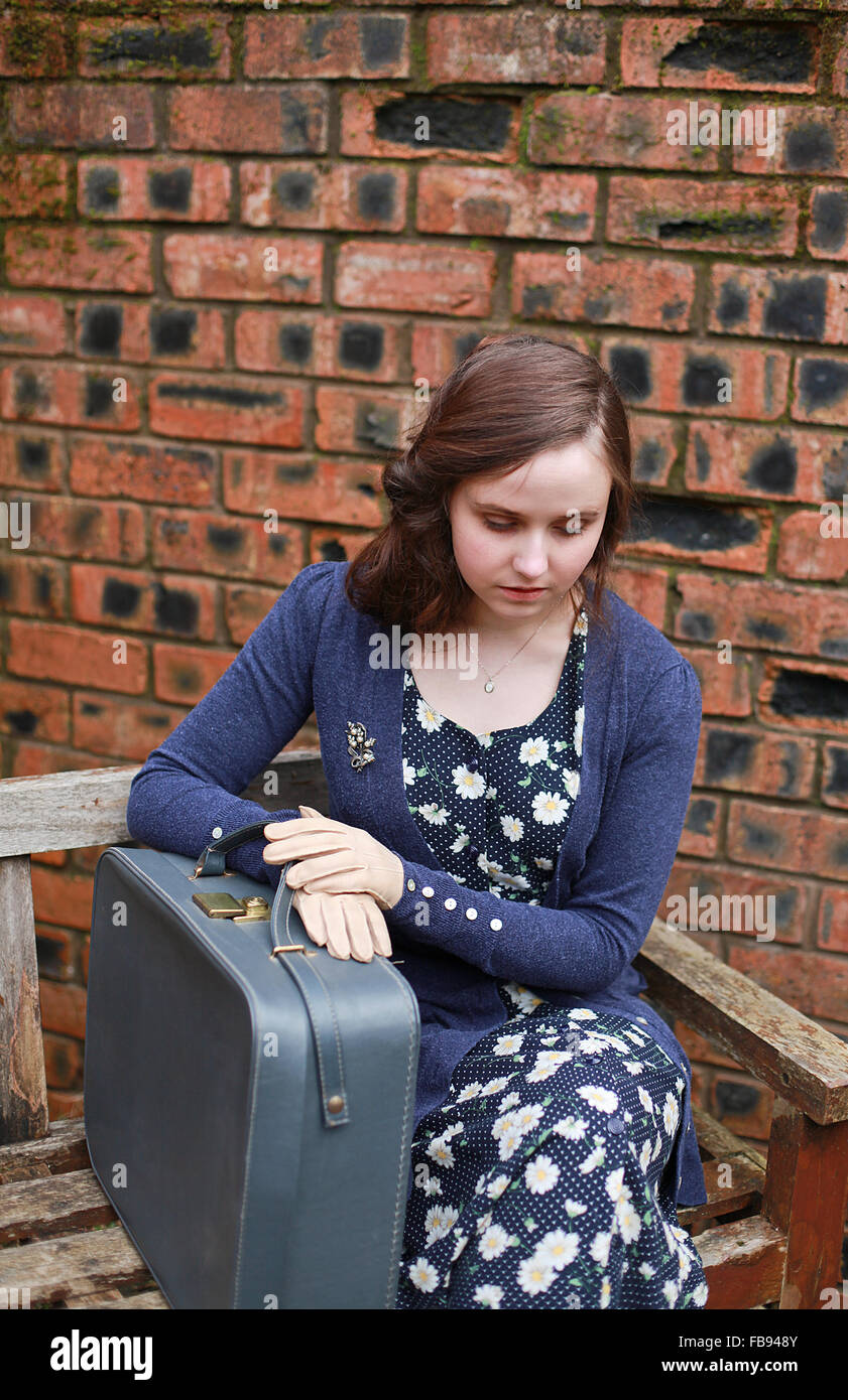 1940s woman sitting on a bench waiting with a suitcase Stock Photo - Alamy