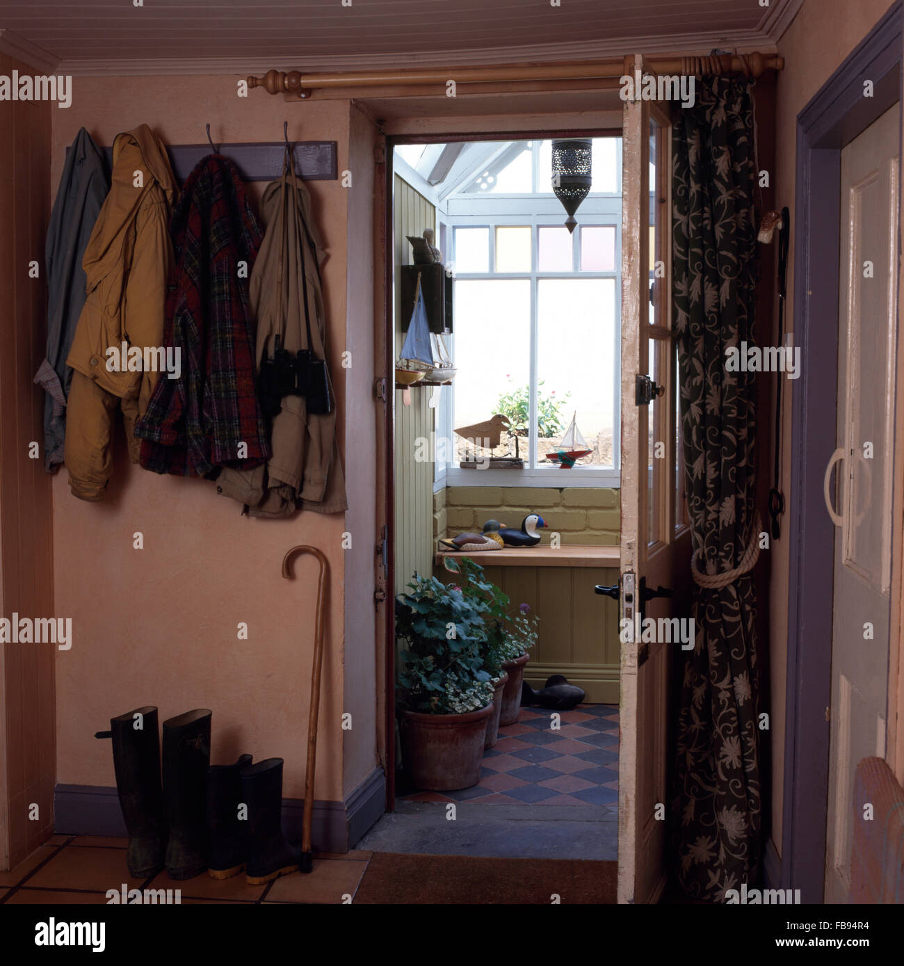 Coats hanging on rack above a row of boots in country hall with door ...