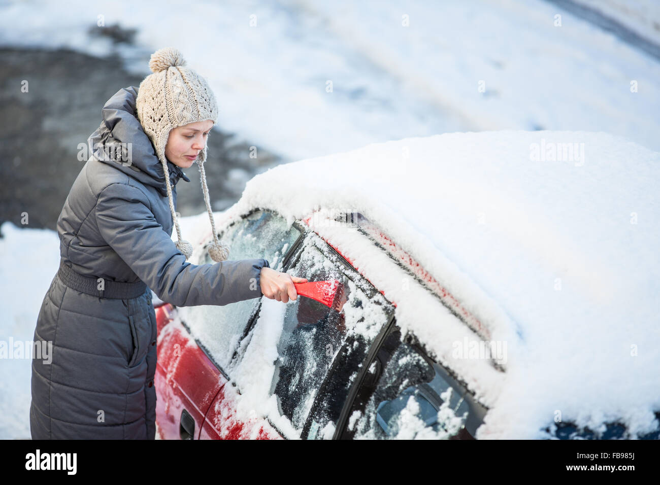 Young woman cleaning her car from snow and frost on a winter morning ...