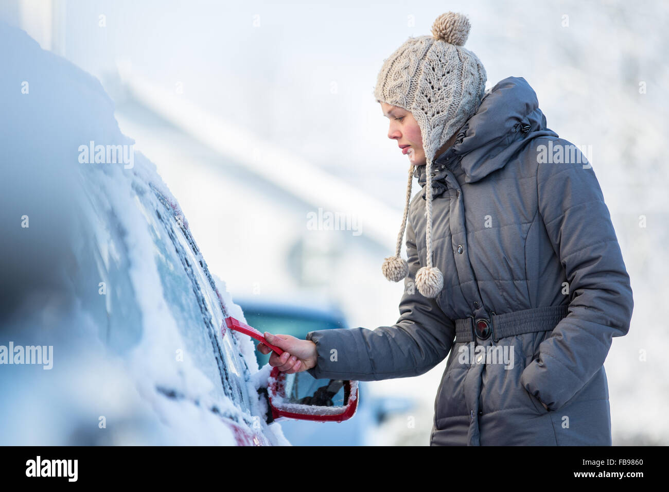 Young woman cleaning her car from snow and frost on a winter morning ...