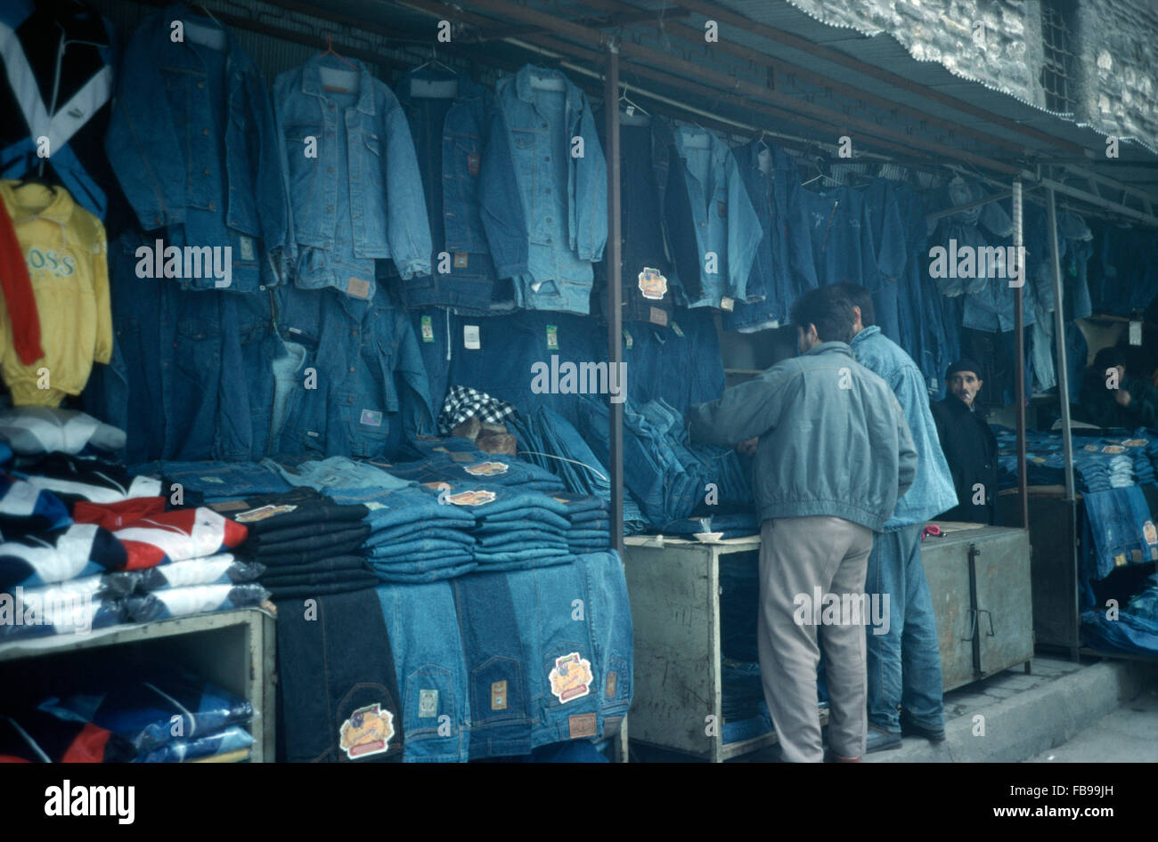 Vendor and customers at a street market stall selling men's denim ...