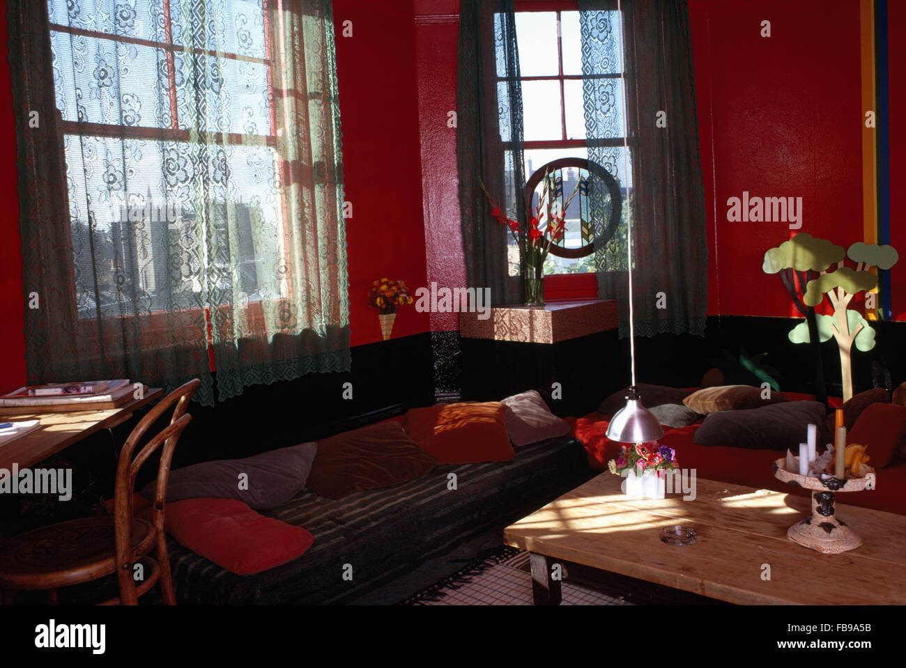 Lace curtains on window above cushions on divan sofa in red sixties ...