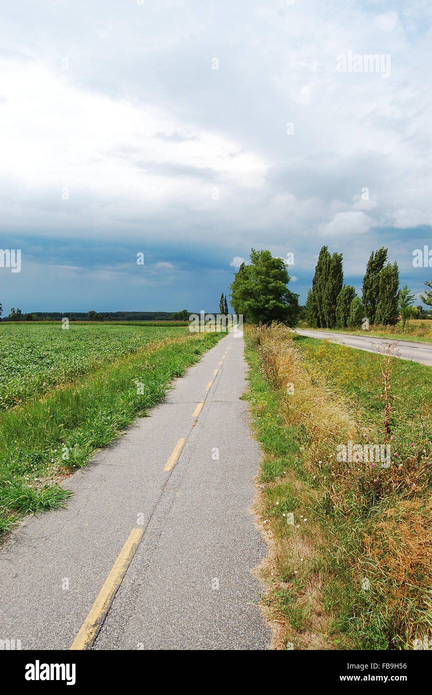 Cycle path along green fields towards ominous clouds Stock Photo - Alamy