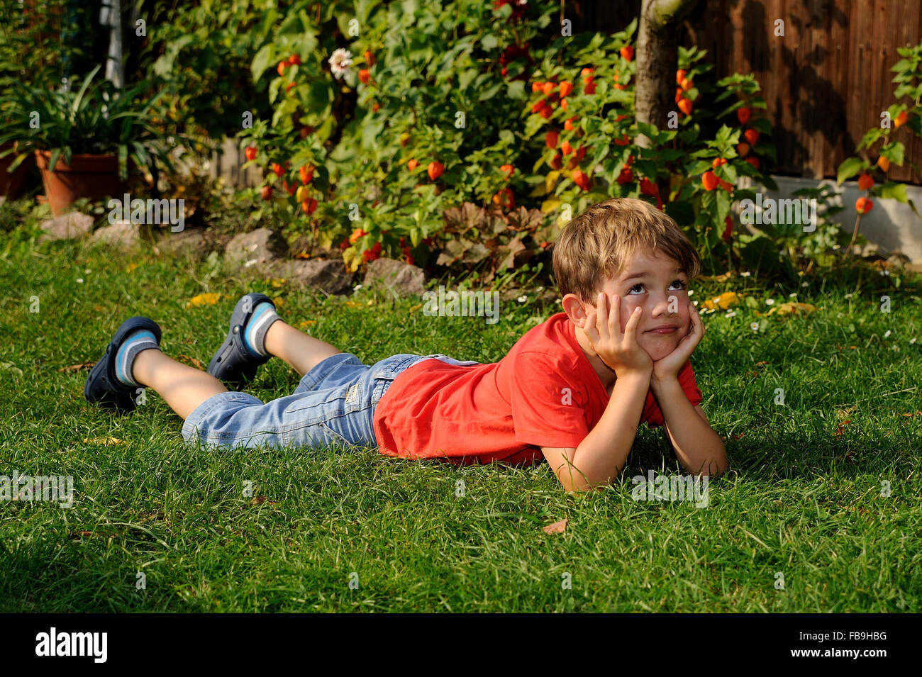 Boy lying on grass, resting head in hands, looking thoughtful Stock ...