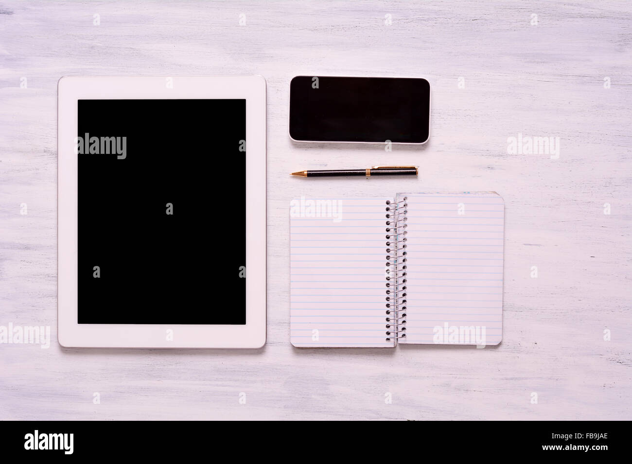 Tablet, notebook, cell phone and pen on white wooden table. View from ...