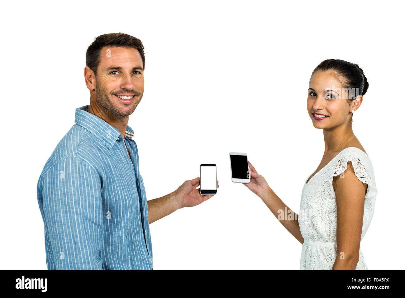 Smiling couple holding smartphones and looking back at camera Stock ...