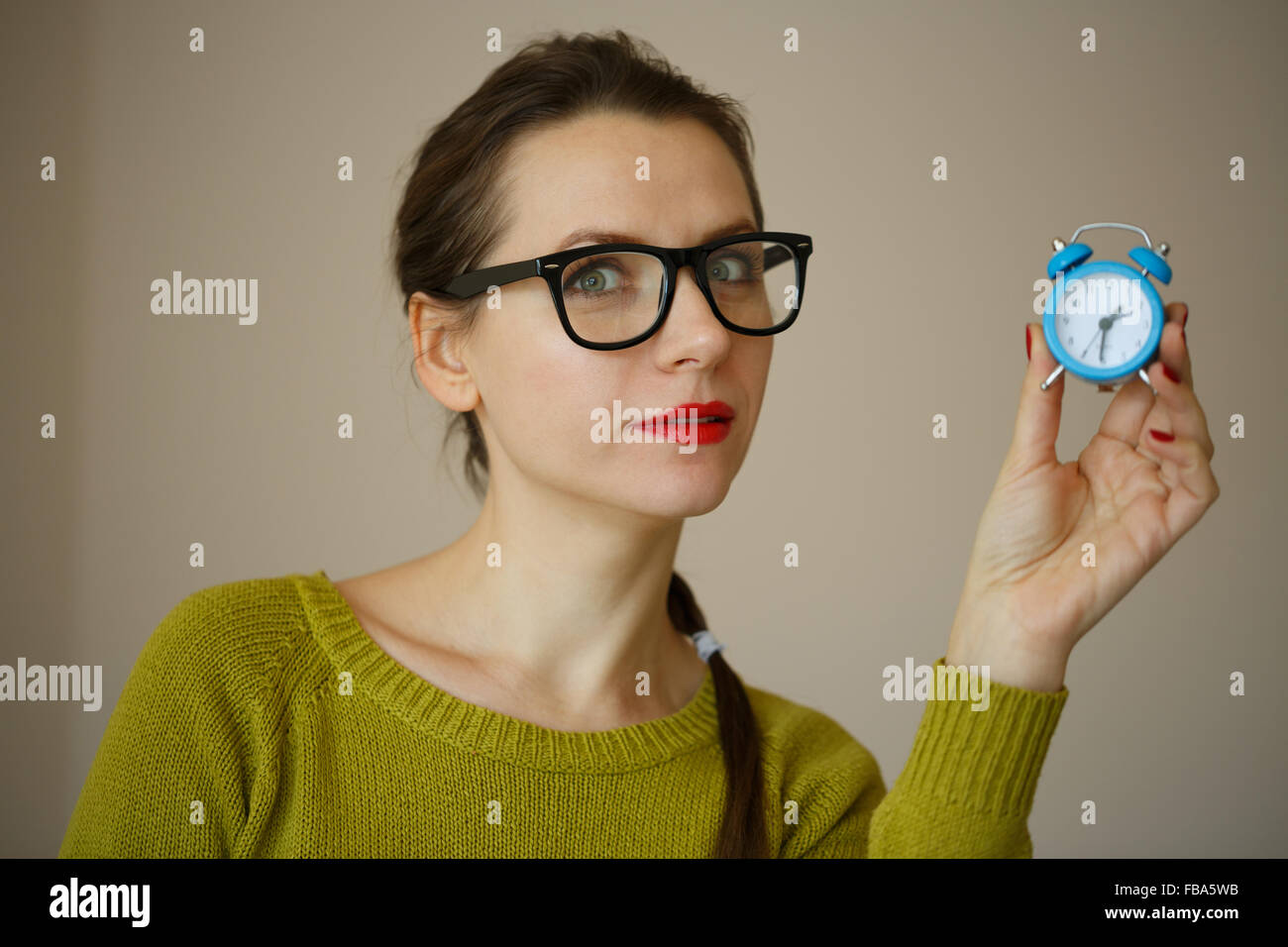 Little blue alarm clock in the hands of an emotional young woman ...