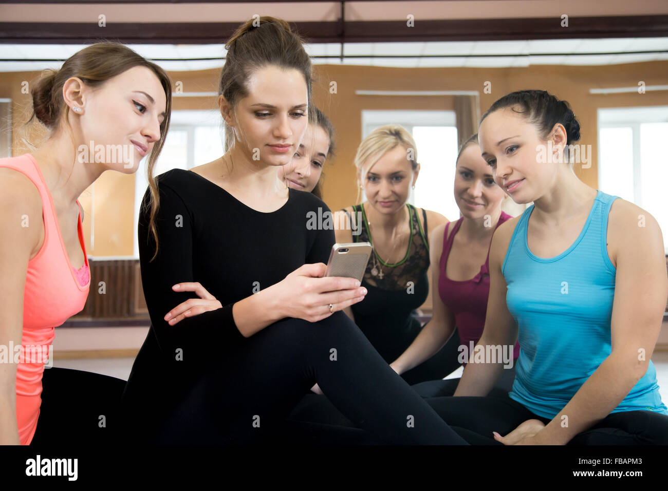 Group of sporty female friends using app on mobile phone, looking at ...