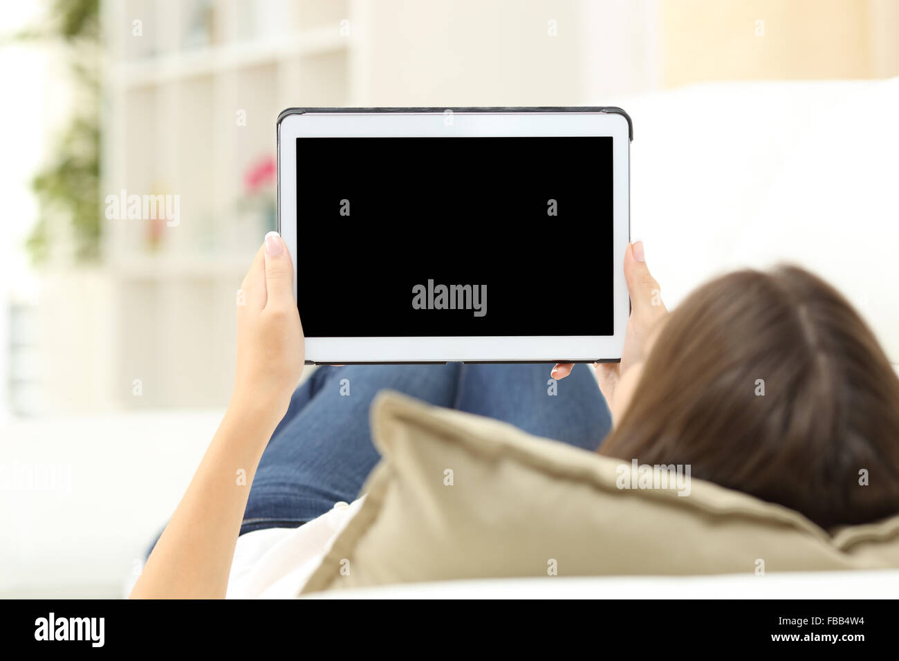 Woman using a tablet and showing a blank screen lying on a couch at ...