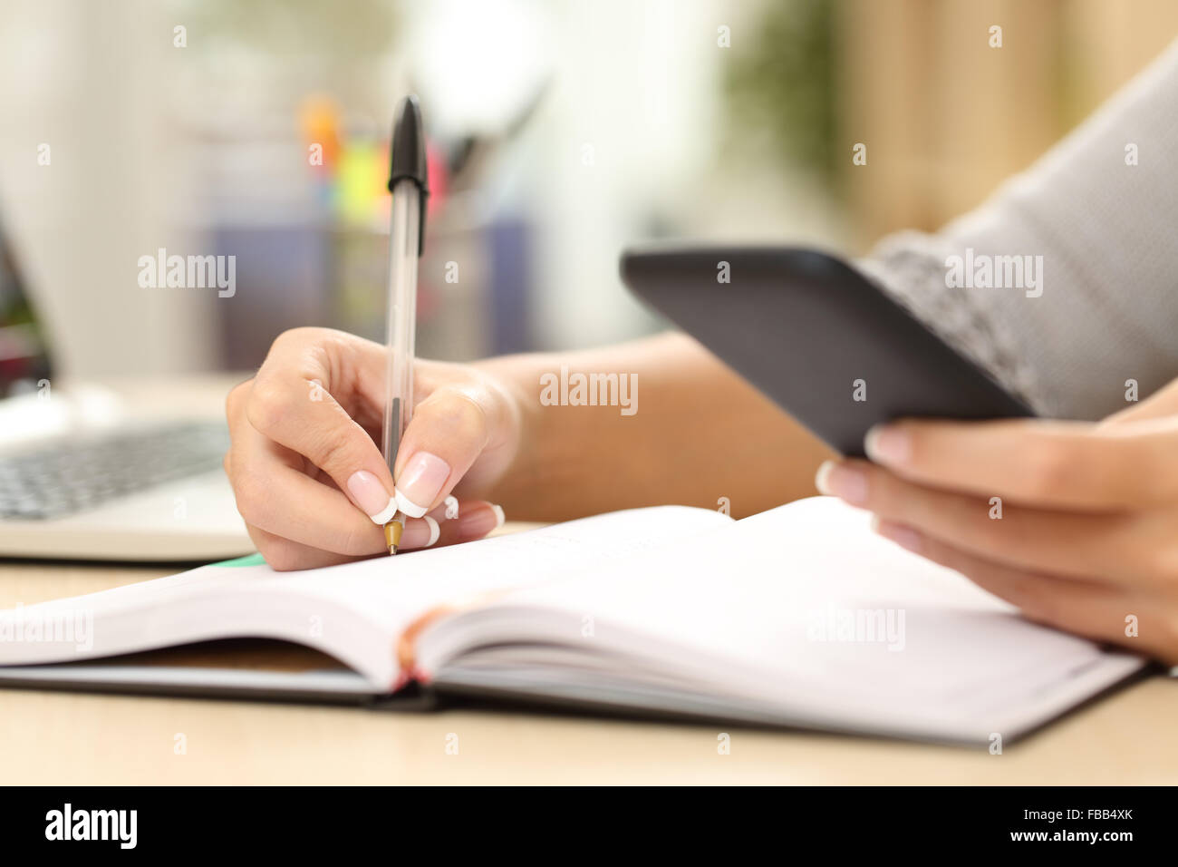 Woman hand writing in agenda consulting a mobile phone on a desk at ...