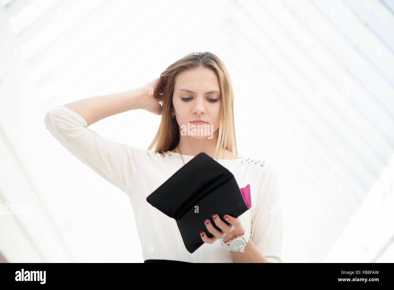 Upset young woman out of money looking into opened wallet in shock ...