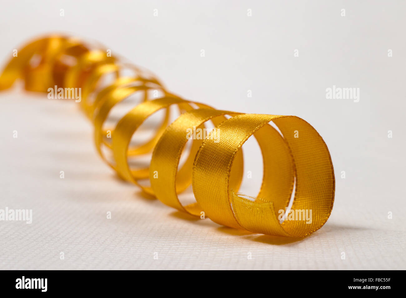 Close-up of golden ribbon spiral in perspective on white background ...