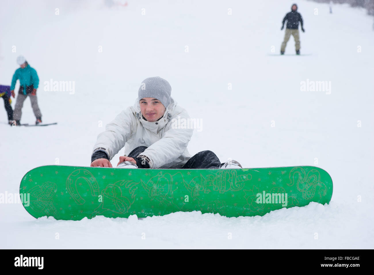 Handsome guy sitting tightening his snowboard in the snow at an alpine ...