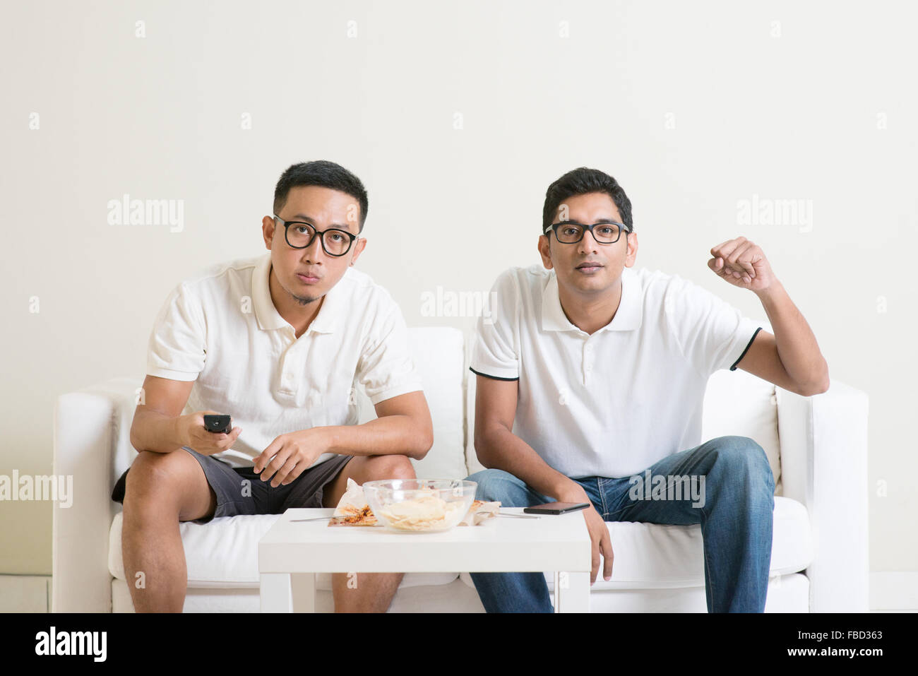 Men sitting on couch watching football match on television, Asian ...