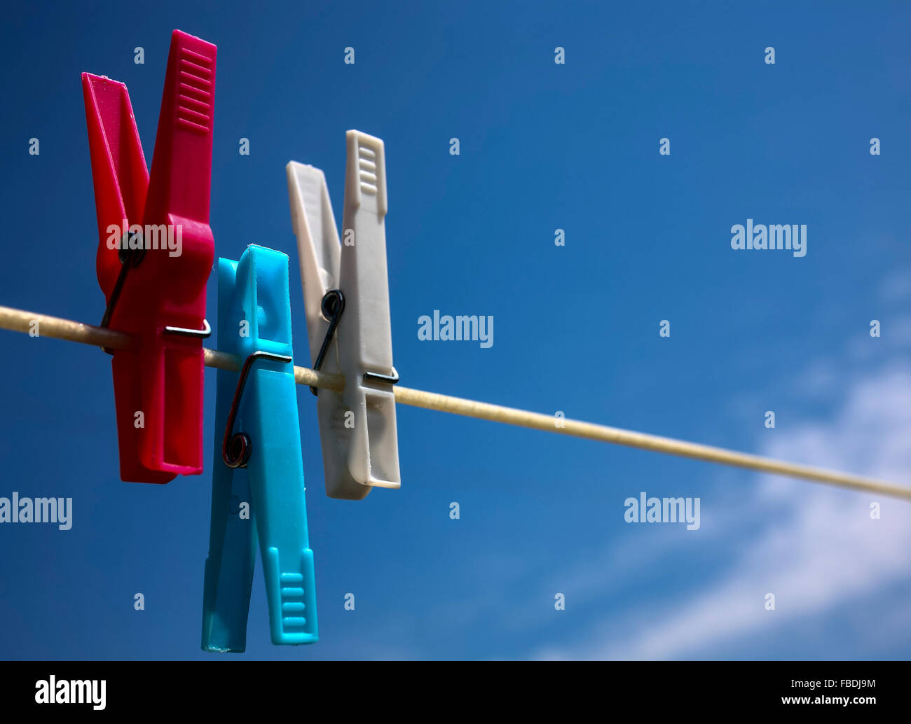 Red blue and white clothes pegs clipped on a washing line with a blue ...