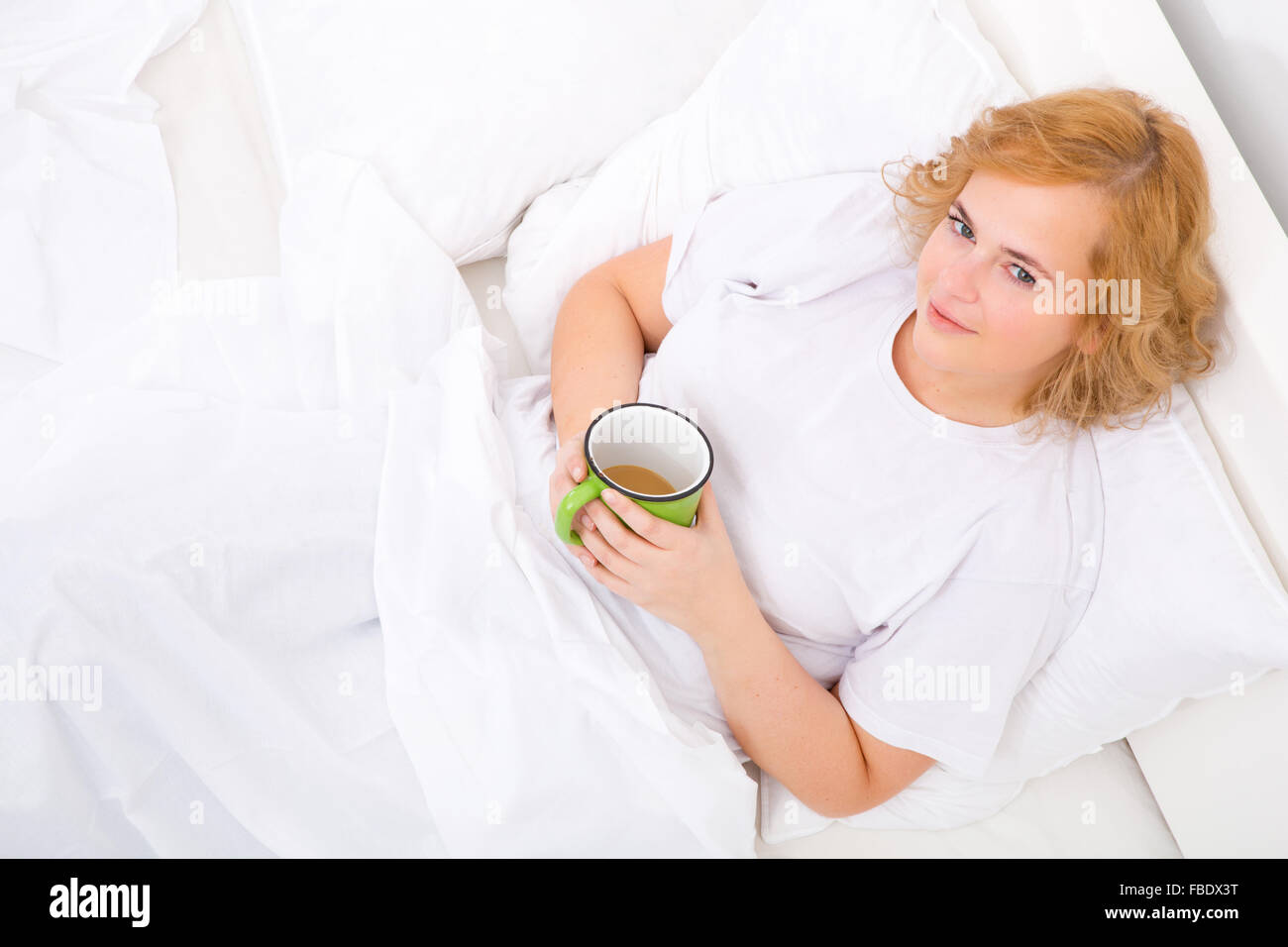 A young plus size woman drinking the first coffee of the day in bed ...