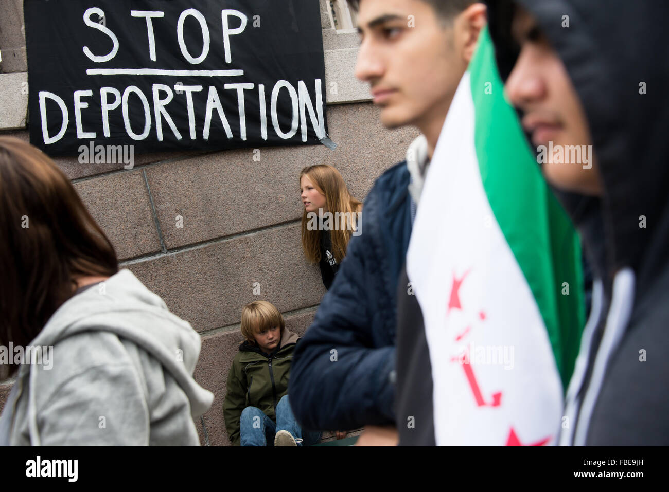 Young men hold a Syrian flag near a banner reading, "Stop Deportation ...