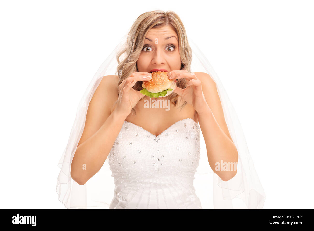 Surprised blond bride eating a sandwich and looking at the camera ...