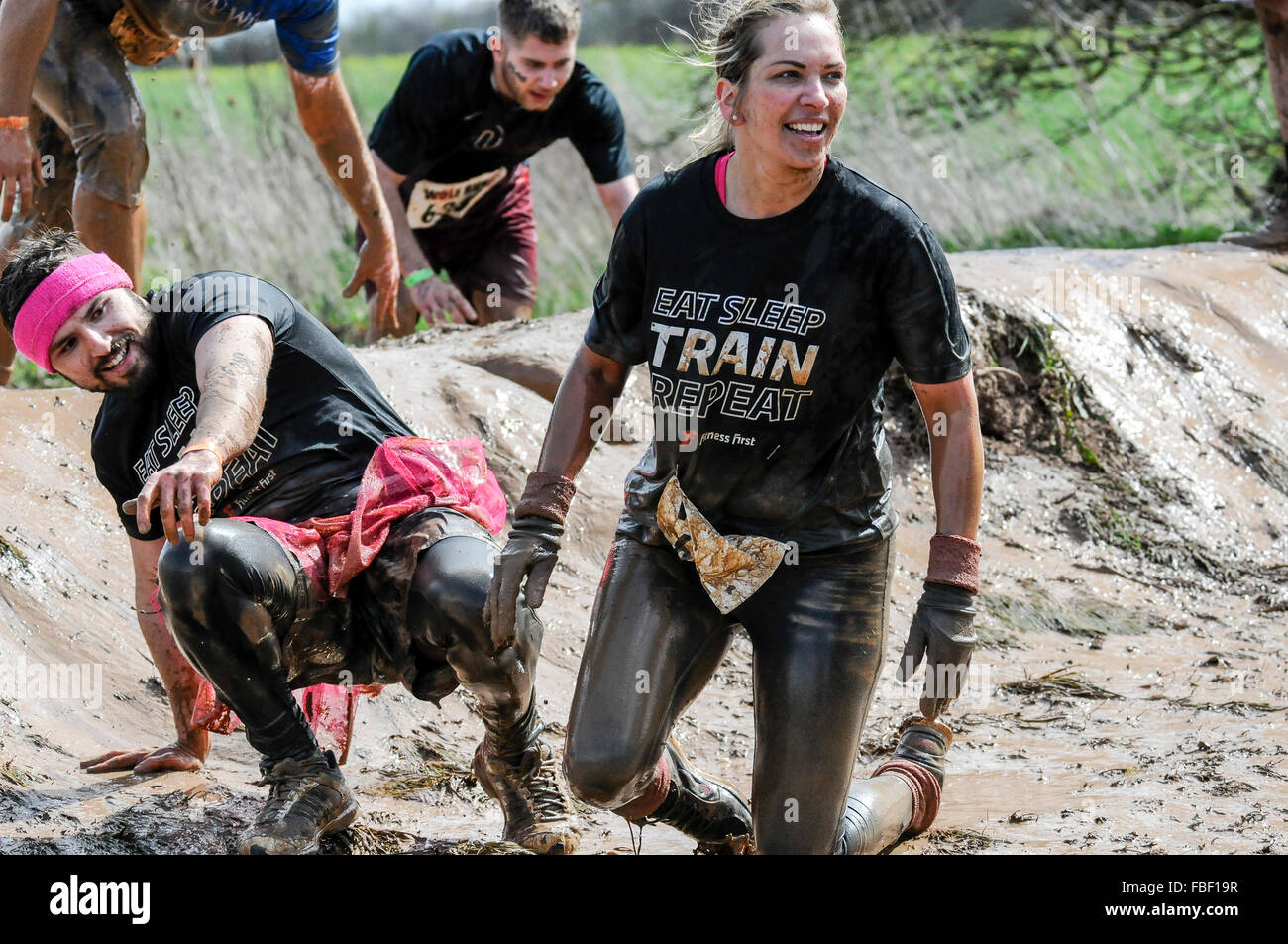 Male and female runners wading through mud lake at obstacle course race ...