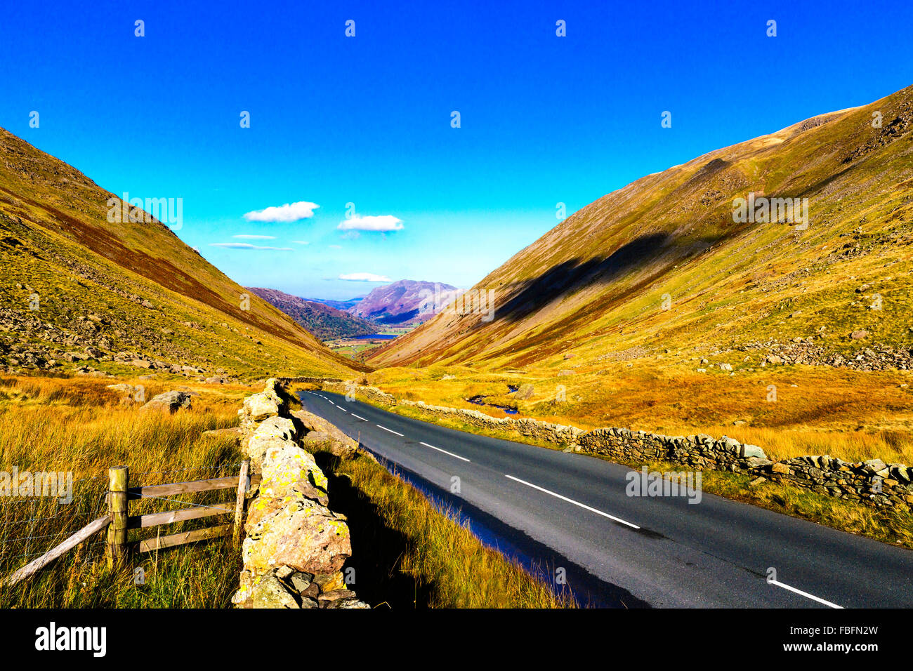 Road descending into a valley with stone wall and wooden gate Stock ...