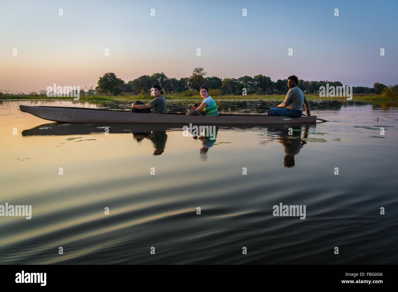 Young travelers and their guide boating at sunset on the Okavango Delta ...