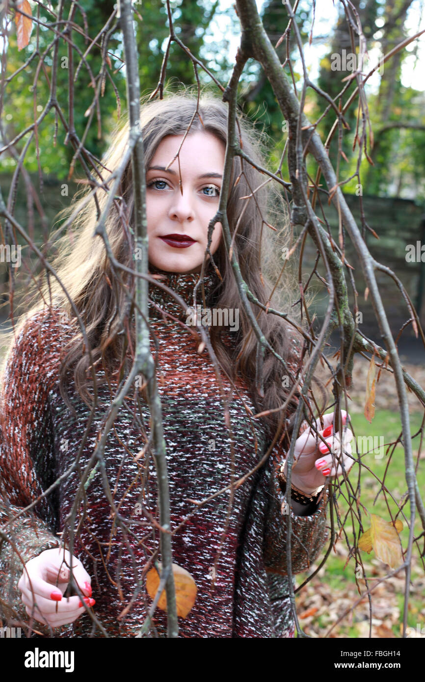 Beautiful modern young woman looking through branches Stock Photo - Alamy