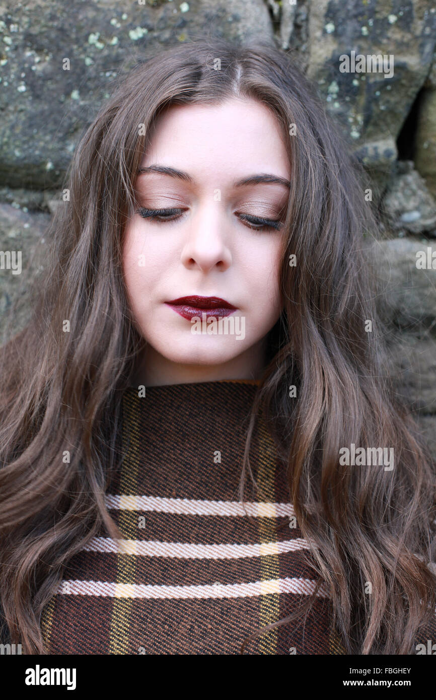 Beautiful young woman leaning on a stone wall with eyes cast down Stock ...