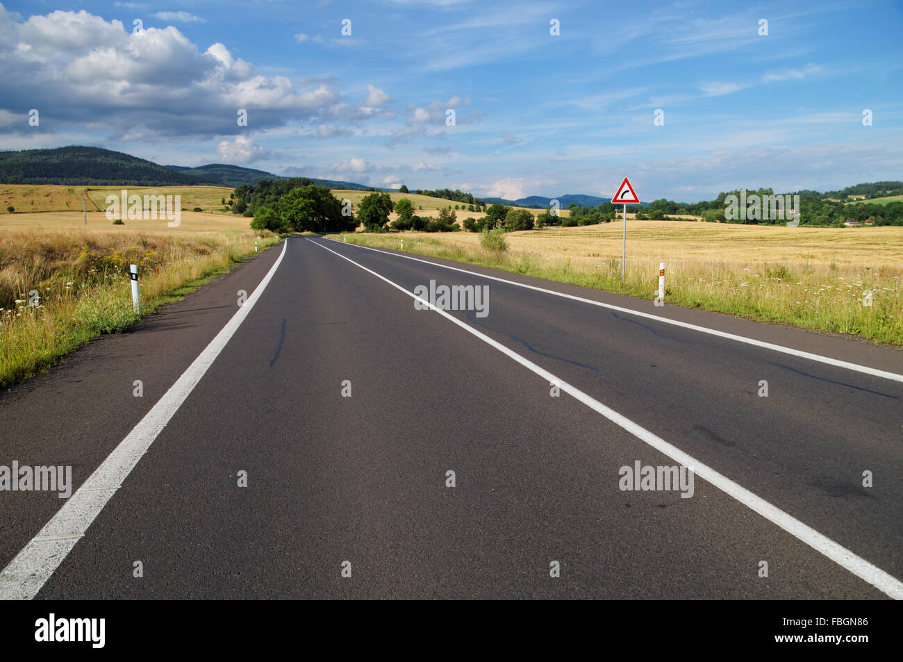 Rural scenery with empty road and traffic sign right bend ahead, in the ...