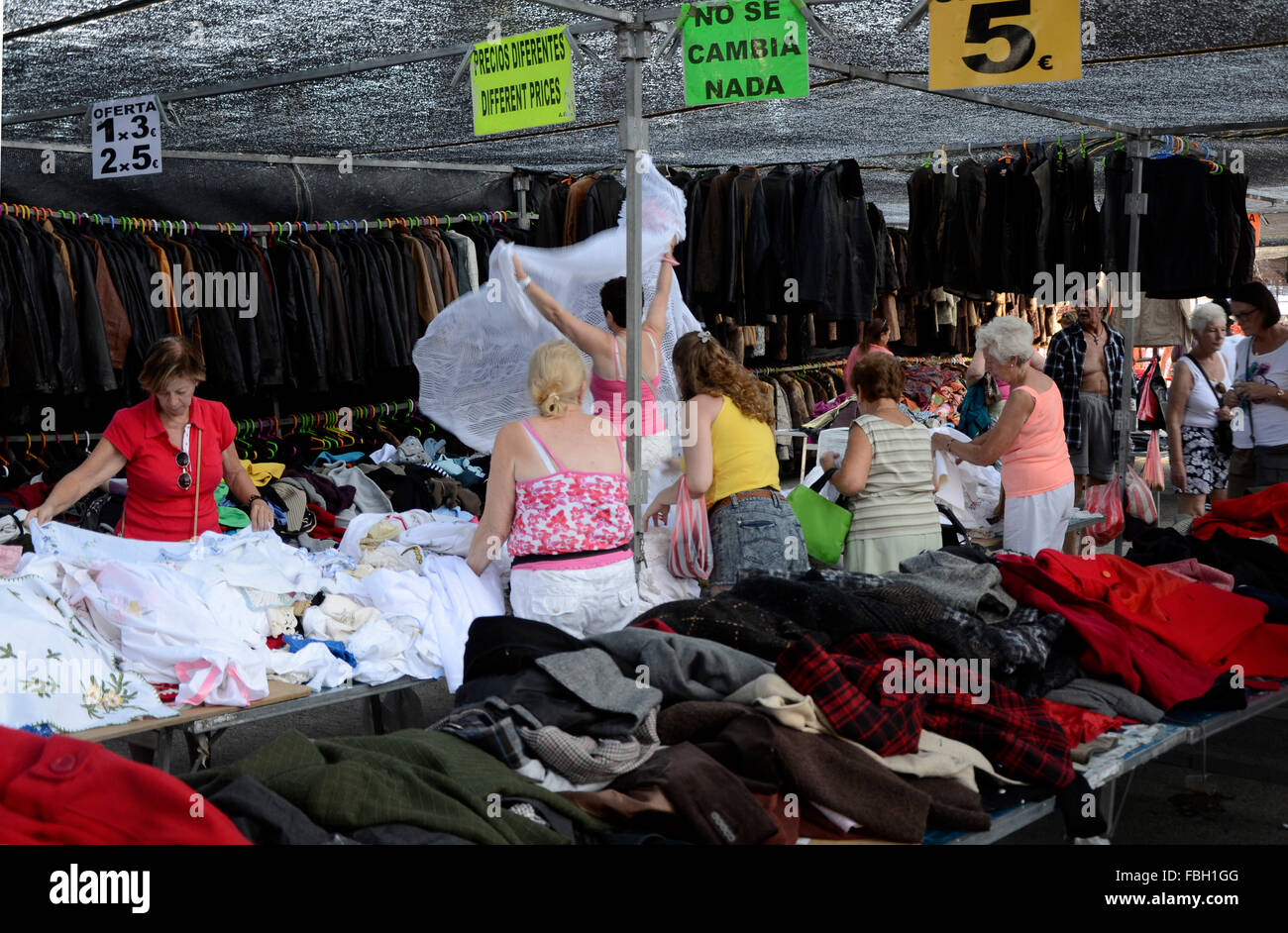 women dig through the offer of a stand selling used clothes at a market ...