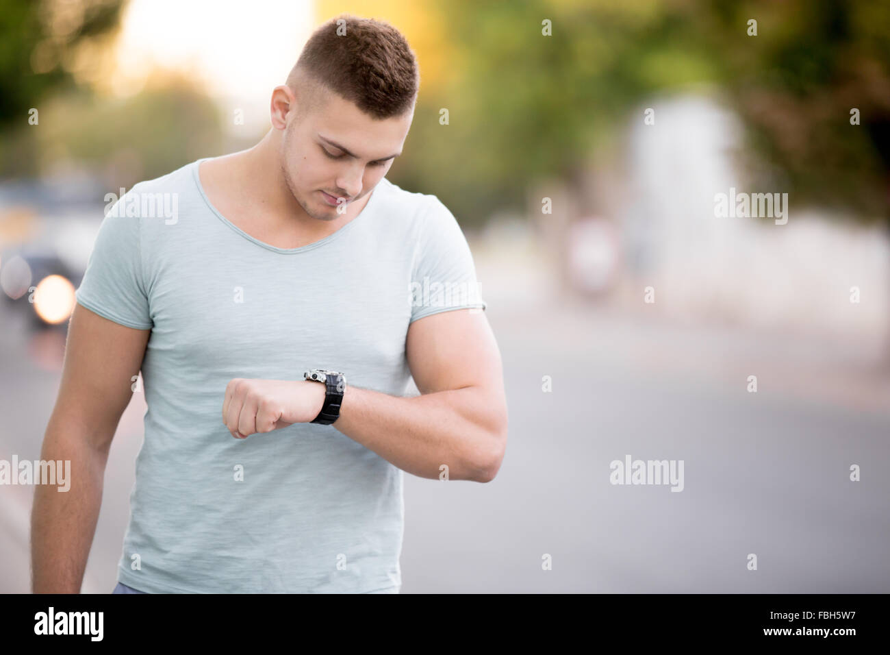 Confident good looking young guy looking at his watch on the street ...