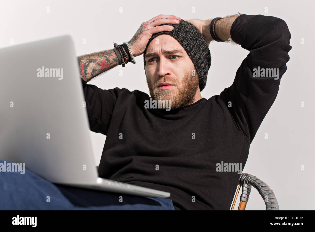 young guy with a beard with a laptop sitting and looking at the monitor ...